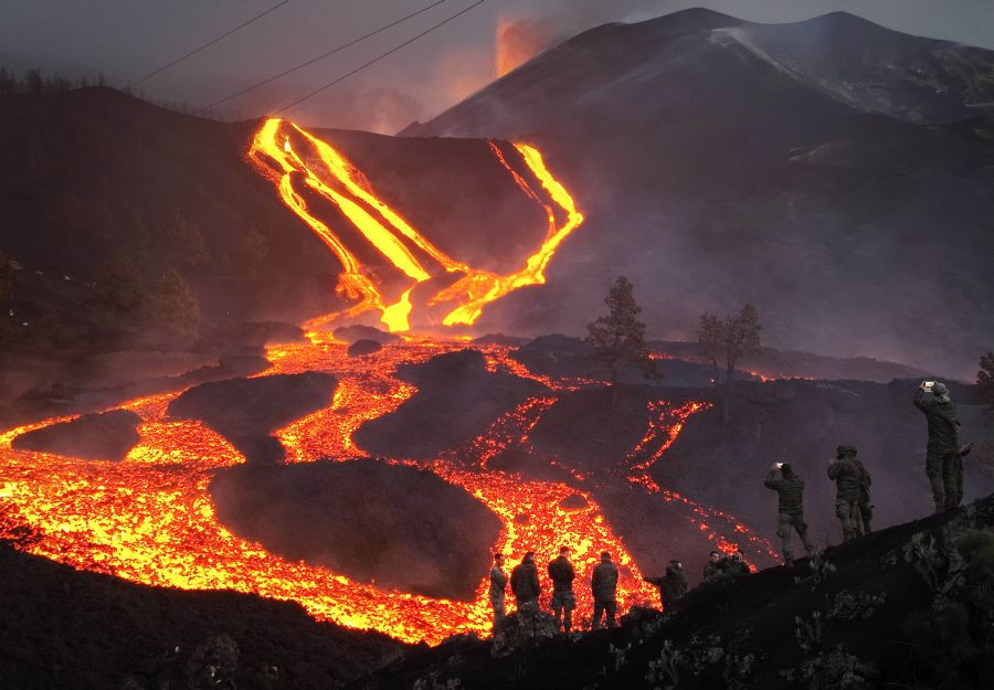 Spanish Army soldiers stand on a hill as lava flows as volcano ...